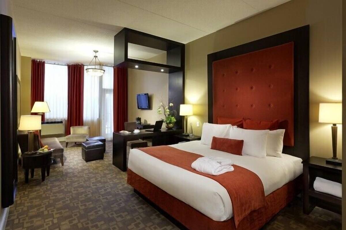 Quarto de hotel com uma cama grande, uma escrivaninha, uma cadeira, uma televisão e uma janela com cortinas.