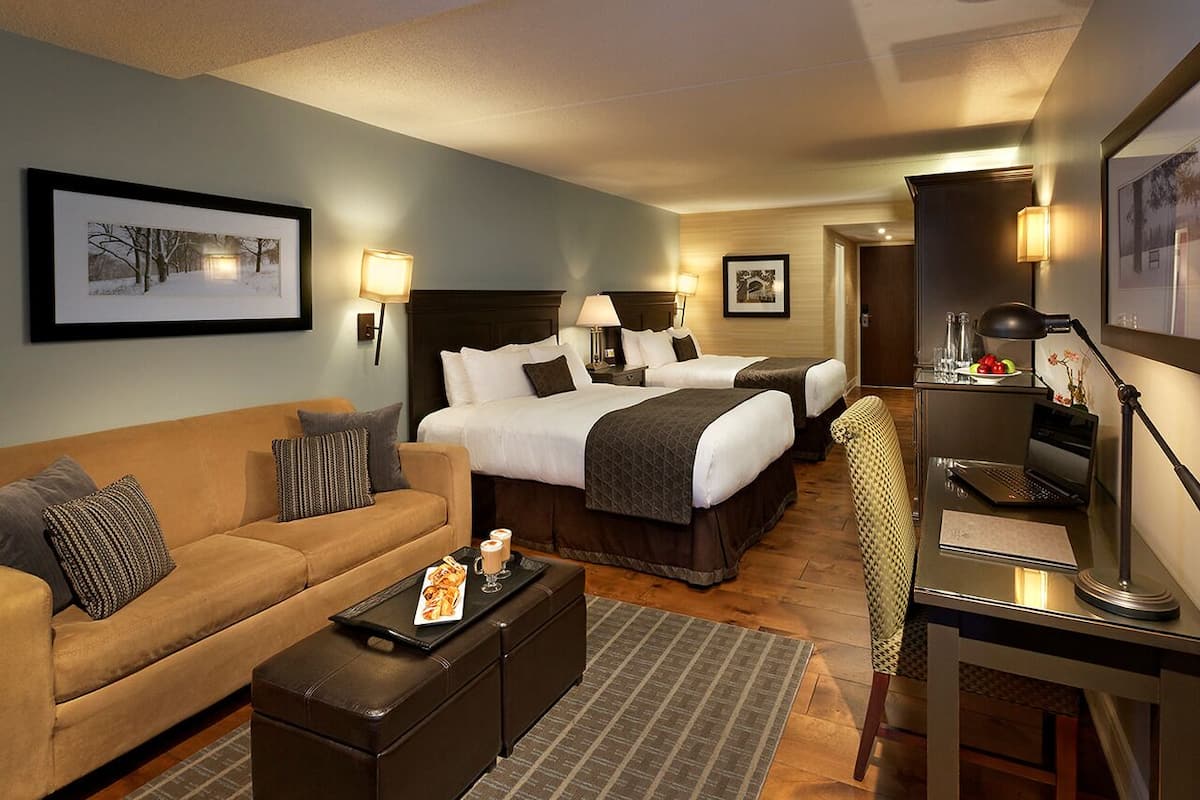 Quarto de hotel com sofá, cama, escrivaninha e laptop, além de uma cadeira.