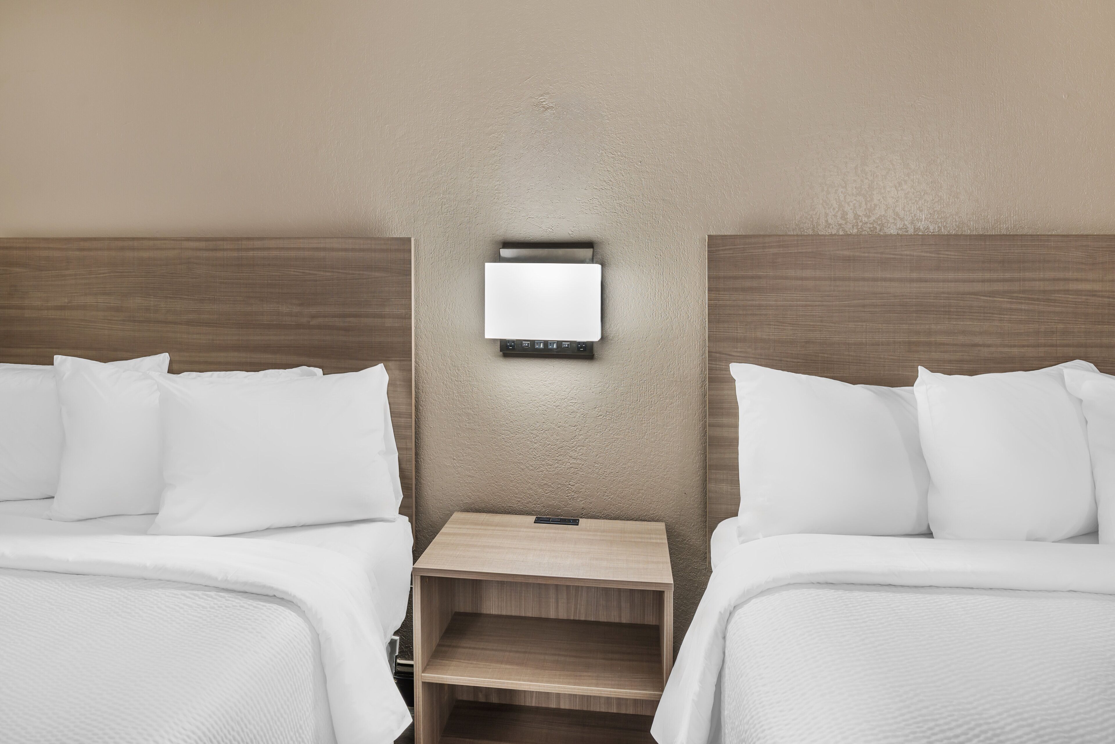 Quarto de hotel com duas camas, uma mesa de cabeceira e painel de controlo na parede.