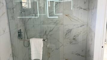 Um chuveiro com paredes de mármore e divisória de vidro, com uma toalha branca pendurada em um suporte de metal.