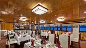 Restaurante com tetos de madeira e mesas preparadas para refeições, com vista para o mar através de grandes janelas.
