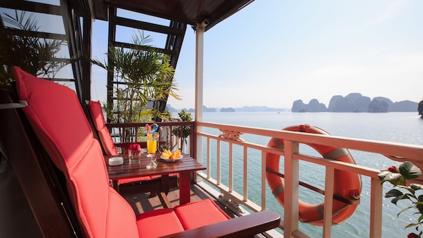 Um terraço com assentos acolchoados em vermelho, uma mesa com bebidas e um buoy de salva-vidas.