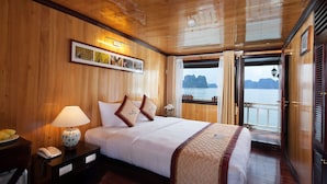 Um quarto com painéis de madeira, uma cama, uma mesa de cabeceira com abajur e vista para o mar através de uma porta aberta.