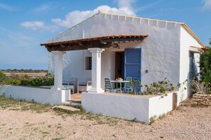 Uma casa branca com telhado em telhas, porta azul e um pequeno alpendre com móveis de exterior.