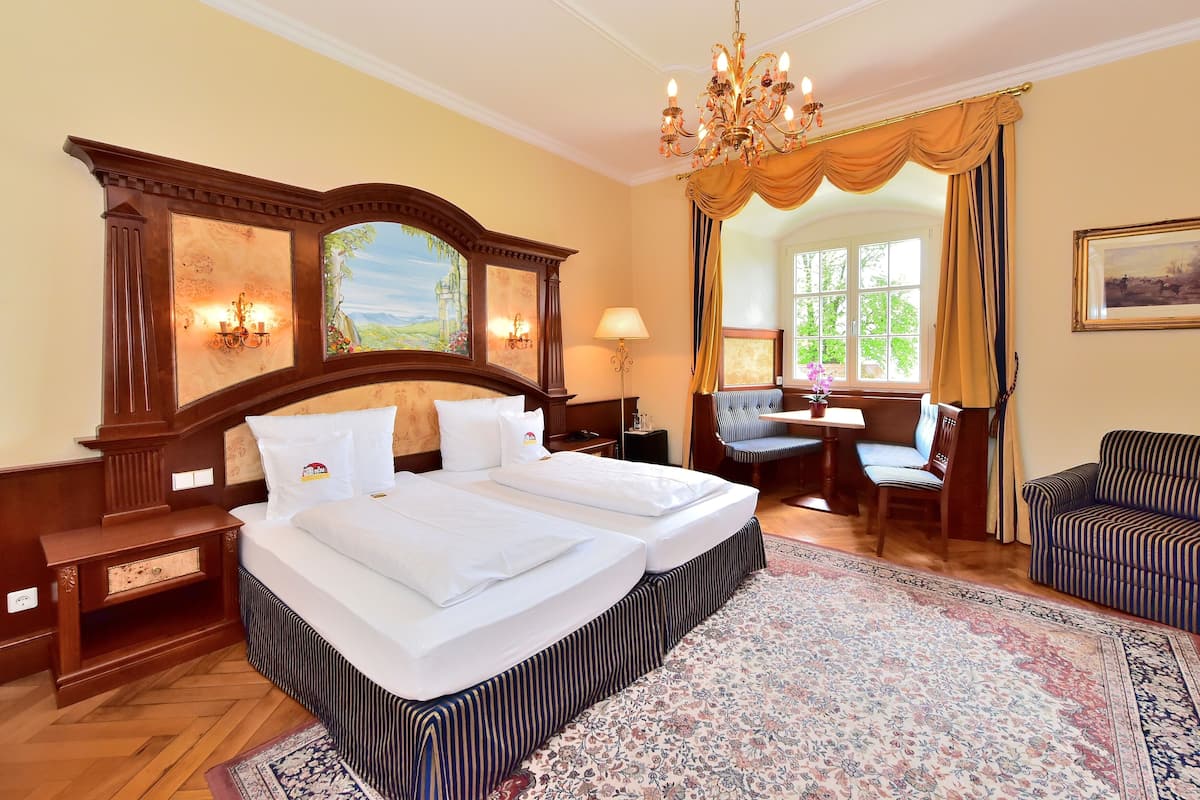 Quarto de hotel com uma cama grande, um candelabro, uma escrivaninha, uma poltrona e um sofá.