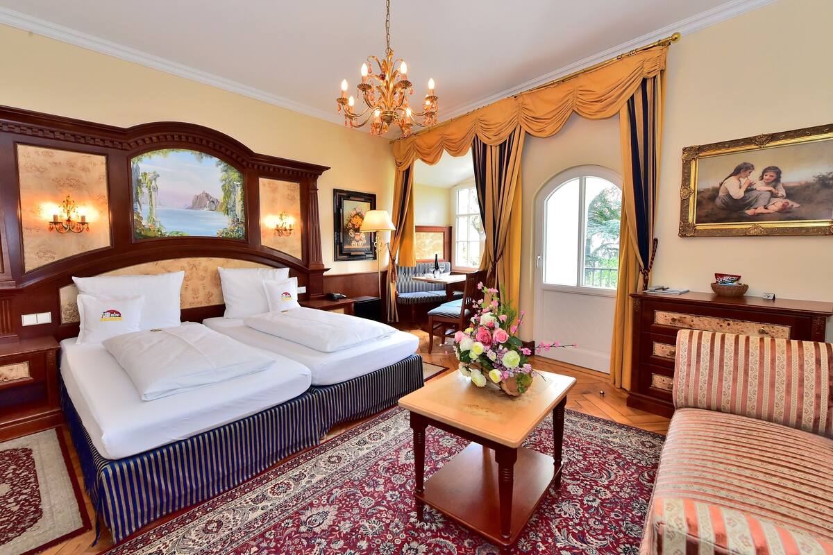 Quarto de hotel com duas camas, um candelabro, uma cômoda de madeira, uma escrivaninha e uma cadeira.