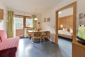 Quarto de hotel compacto com cama, mesa de jantar com cadeiras, televisão e banheiro visível por uma porta aberta.