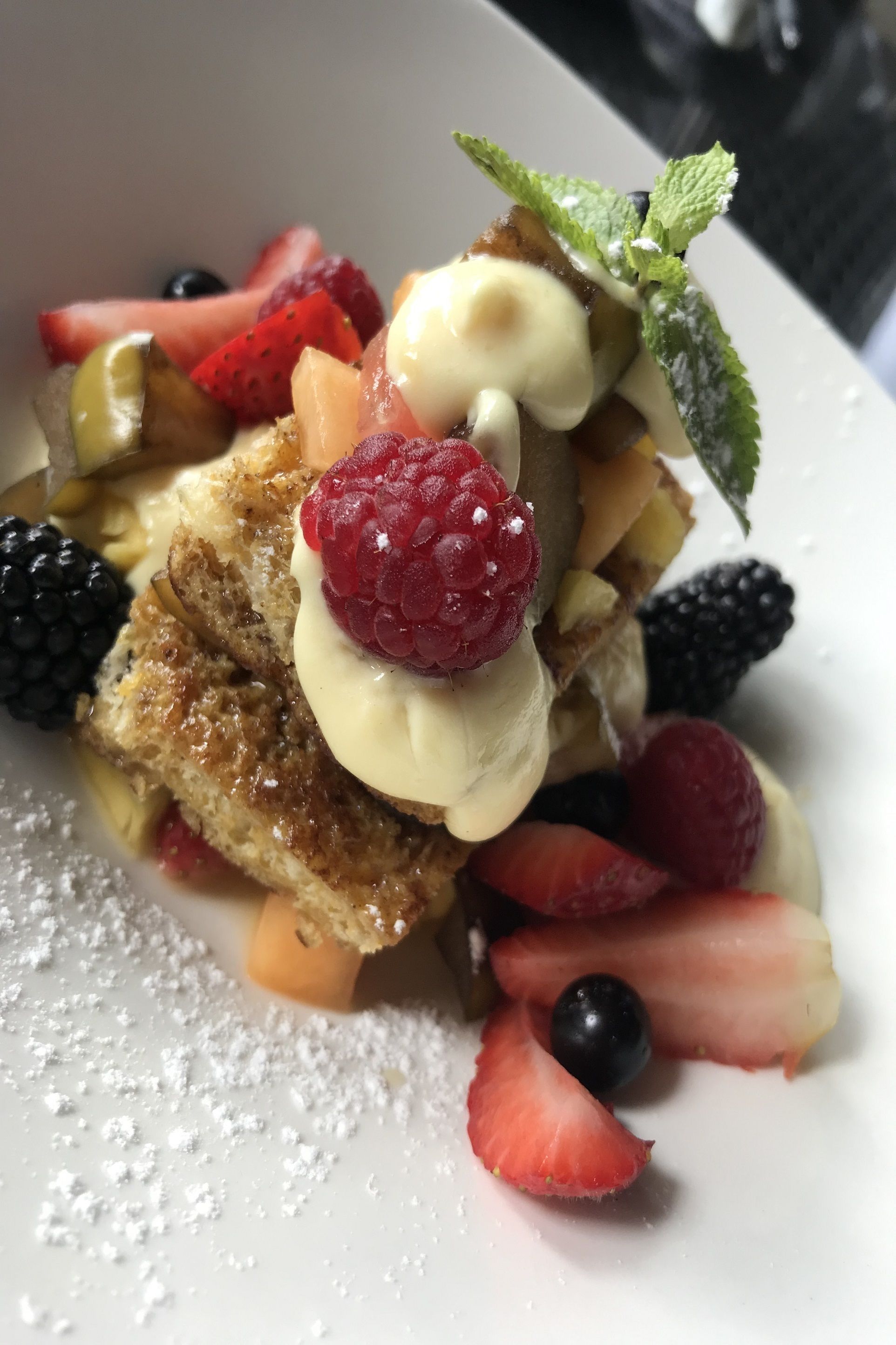 Um prato de sobremesa com panquecas, frutas vermelhas frescas e um ramo de hortelã.