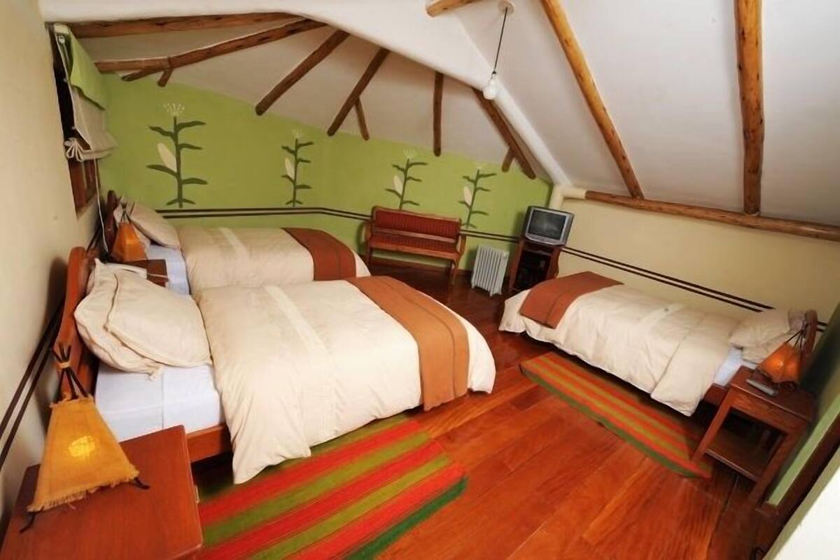 Um quarto aconchegante com duas camas, uma televisão pequena e estrutura de teto em madeira.