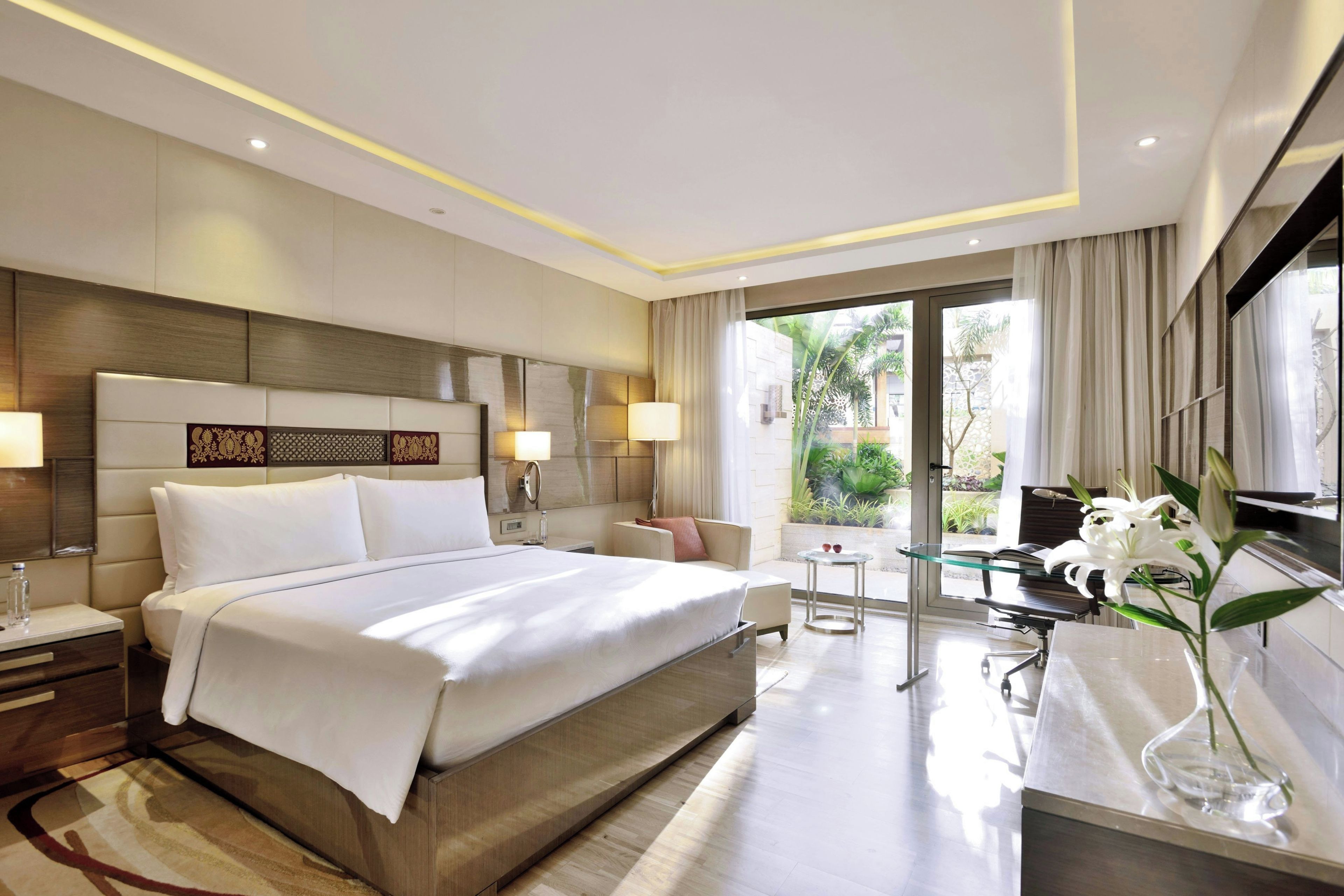 Quarto de hotel moderno com uma cama grande, mesas de cabeceira, escrivaninha e vista para o exterior.