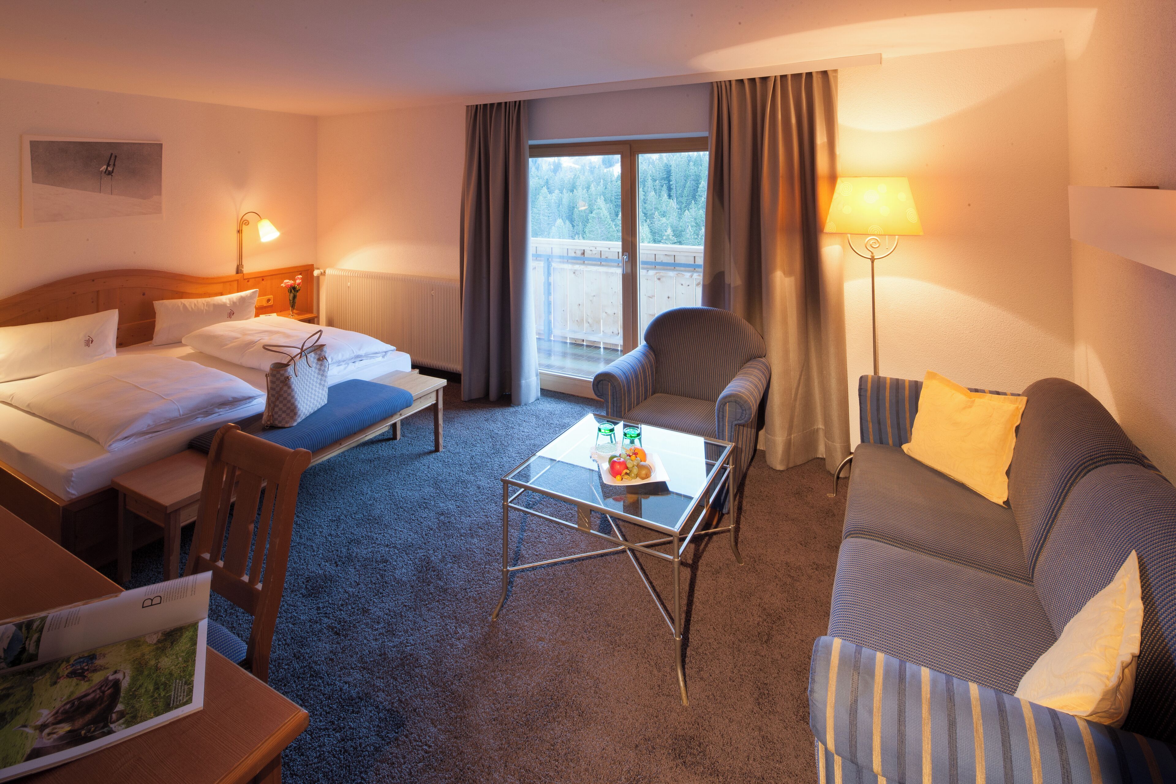 Quarto de hotel com cama, sofá, cadeira, mesa e vista para uma varanda.
