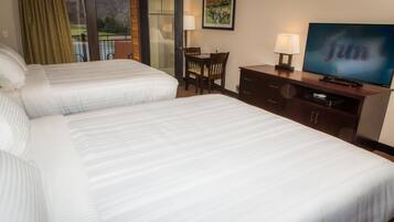 Quarto de hotel com duas camas, uma escrivaninha, televisão e janela com vista para árvores.