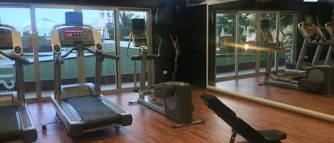 Uma academia com esteiras, elípticos e um banco.