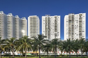 Uma fileira de edifícios residenciais altos com varandas, cercada por palmeiras.
