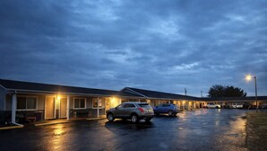 Um motel com vários quartos, estacionamento e chão molhado, provavelmente após chuva.
