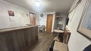 Um saguão de hotel com uma mesa de recepção de madeira, uma mesa redonda, um relógio e um cabideiro.
