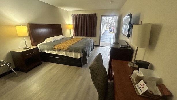 Quarto de hotel com cama, mesas de cabeceira, escrivaninha, cadeira, televisão e janela com cortinas.