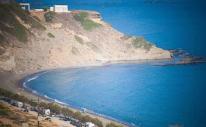 Vista costeira com praia arenosa, falésias rochosas e mar azul límpido.