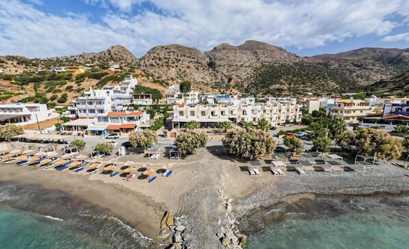 Uma cidade costeira com edifícios, uma praia e montanhas ao fundo.