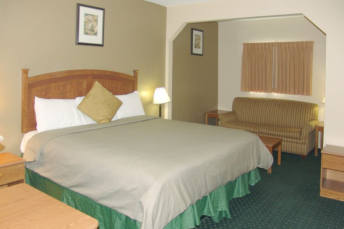Quarto de hotel com cama, cadeira, mesa de cabeceira e janela com cortinas.
