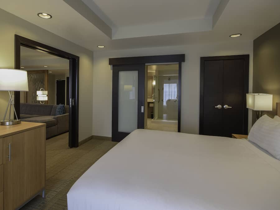Quarto de hotel com uma cama grande, uma mesa com luminária, um guarda-roupa e um espelho.