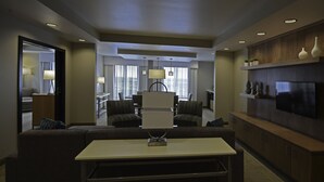 Quarto de hotel moderno com área de estar, mesa de jantar e televisão.