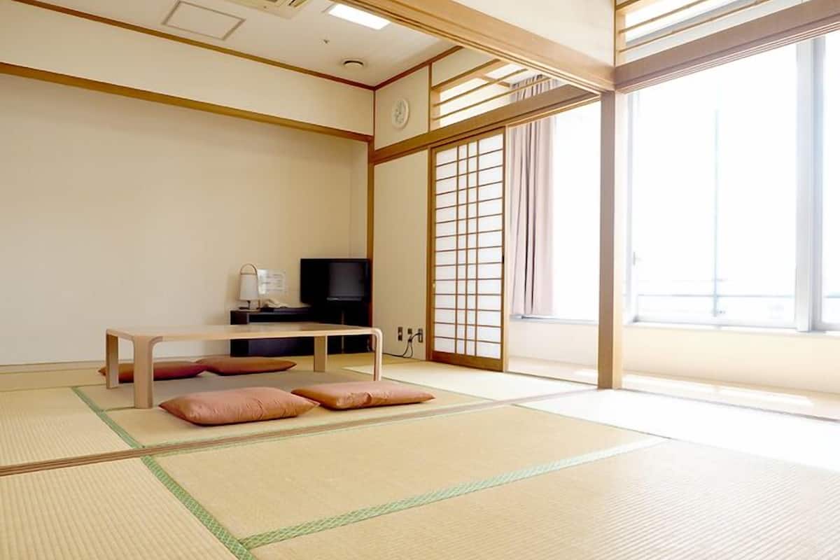 Um quarto com esteiras de tatame, uma cama futon, uma televisão e uma porta deslizante.