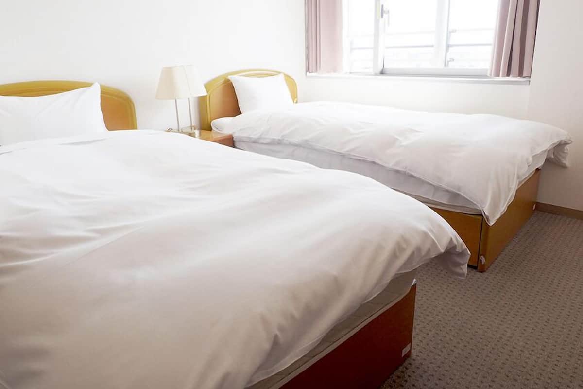 Quarto de hotel com duas camas, janela com cortinas e uma luminária na mesa de cabeceira.