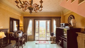 Quarto com lustre, lareira, escrivaninha com telefone, cadeira e vista pelas portas de vidro.