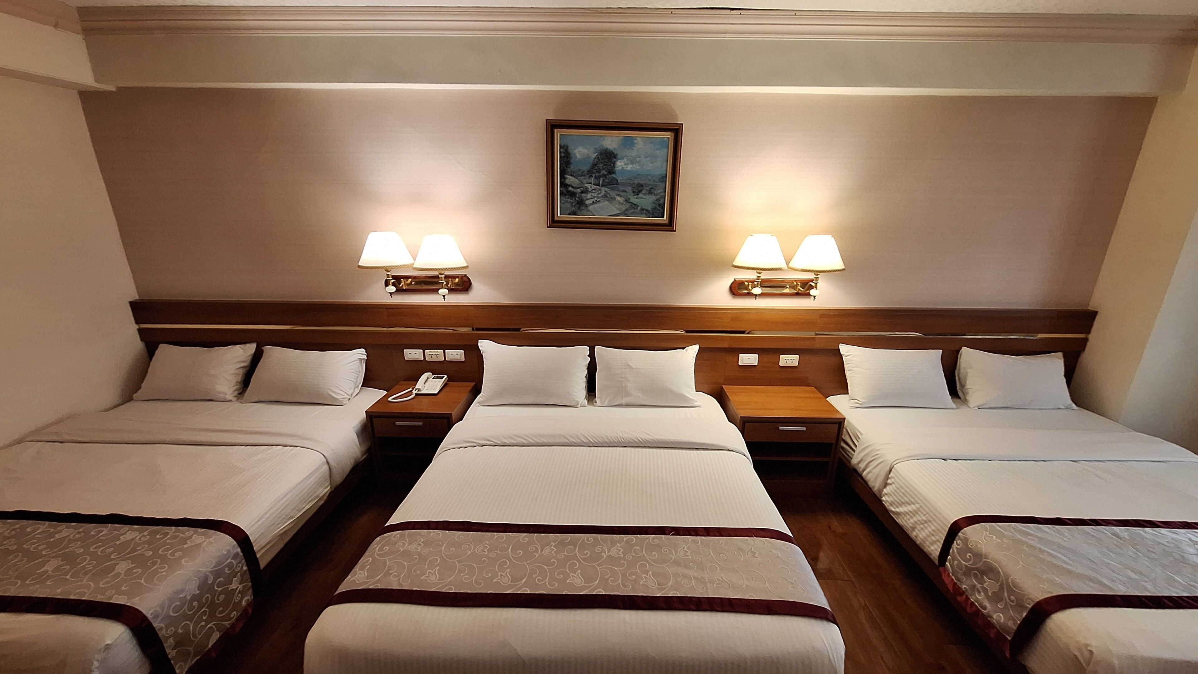Quarto de hotel com quatro camas, duas luminárias de cabeceira, um quadro na parede e um telefone no criado-mudo.
