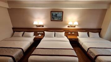 Quarto de hotel com quatro camas, duas luminárias de cabeceira, um quadro na parede e um telefone no criado-mudo.