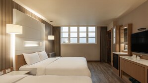 Quarto de hotel com duas camas, televisão, escrivaninha e janela com vista.