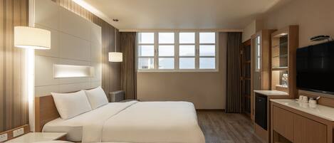 Quarto de hotel com duas camas, televisão, escrivaninha e janela com vista.