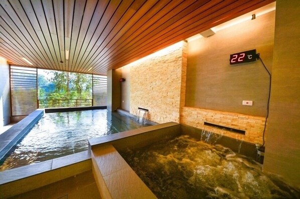 Piscina interior moderna com teto de madeira, visor digital de temperatura e vista para o verde lá fora.