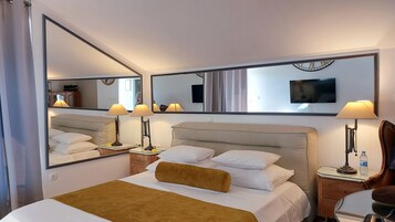 Quarto de hotel com uma cama grande, duas luminárias de cabeceira, uma TV e um espelho.