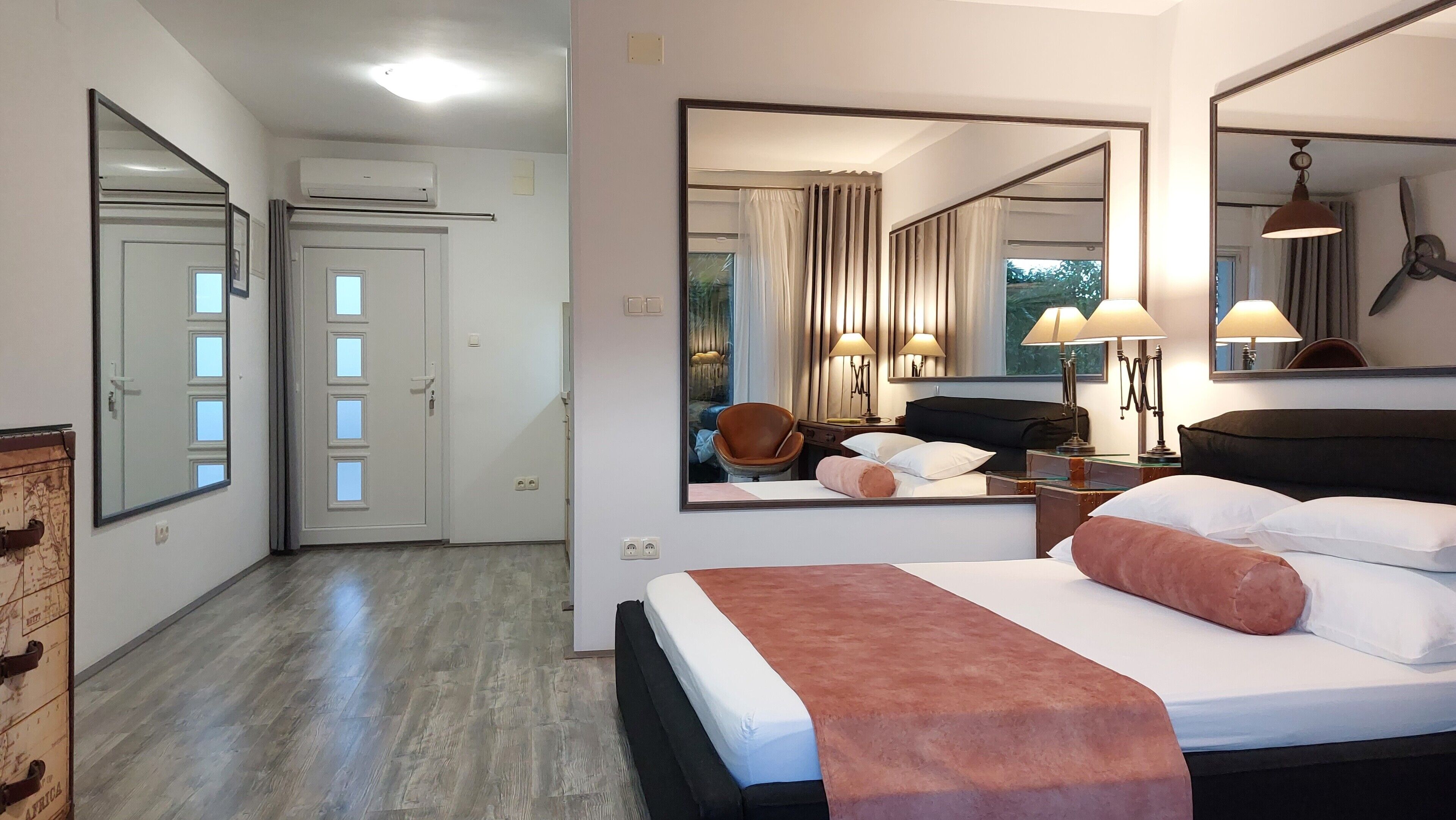 Quarto de hotel com uma cama grande, uma escrivaninha com cadeira, um espelho e um guarda-roupa.