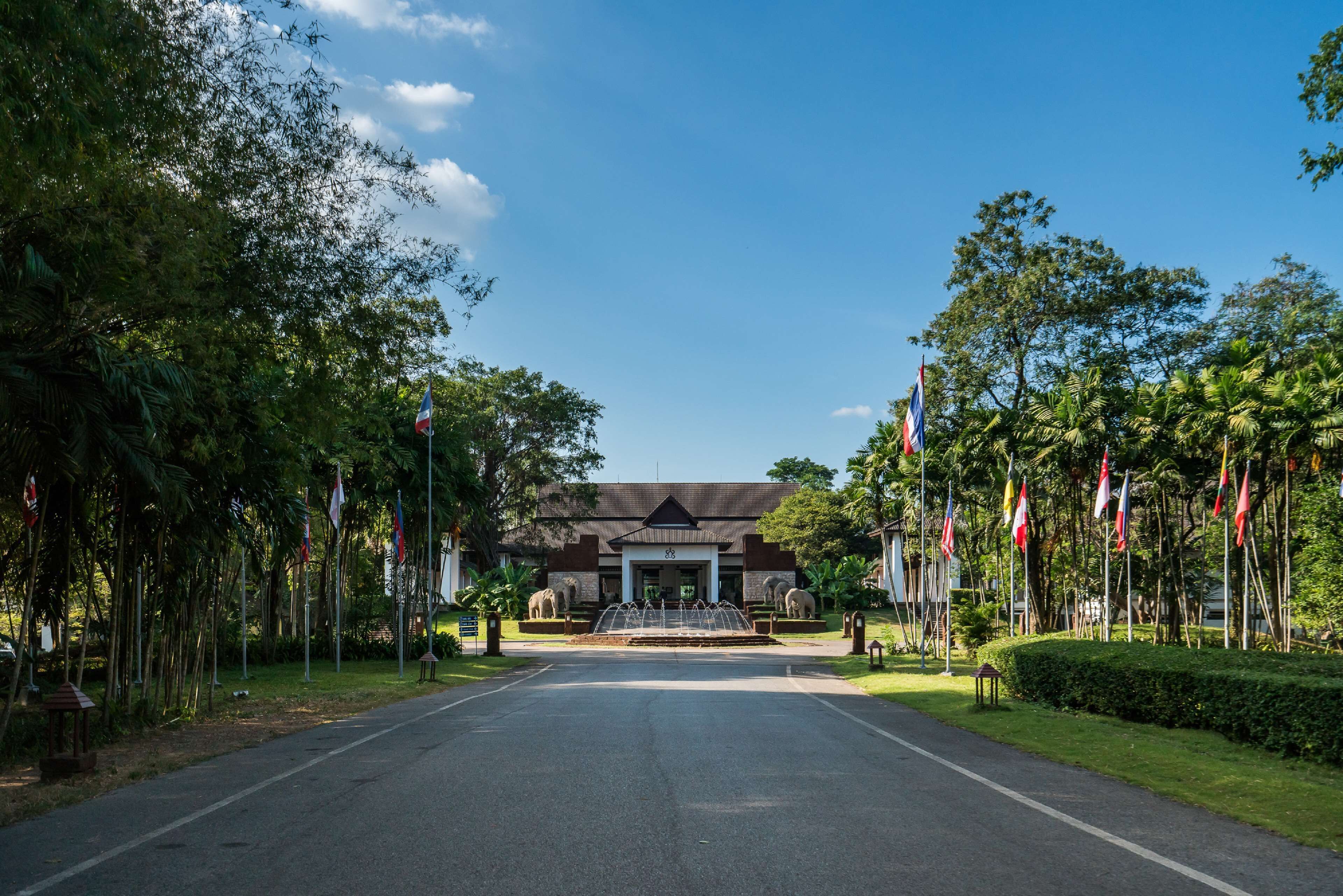 Um edifício com entrada central, cercado por bandeiras e palmeiras.