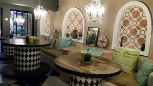 Uma área de bar com mesas redondas, almofadas estampadas e painéis decorativos na parede.