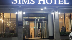 Entrada do HOTEL SIMS com sinalização iluminada e porta de vidro.
