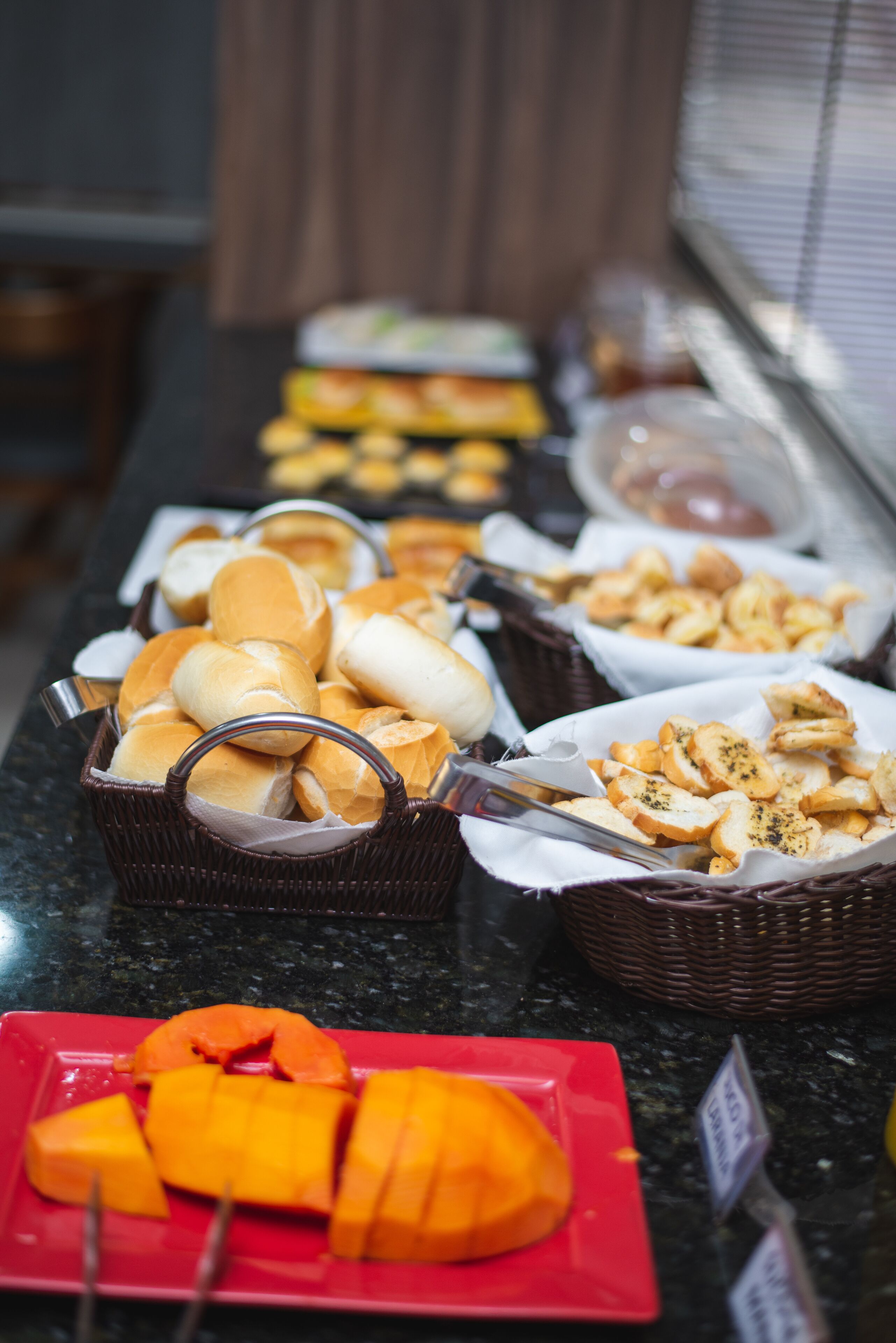 Buffet com diversos alimentos, incluindo pão, doces e frutas fatiadas.