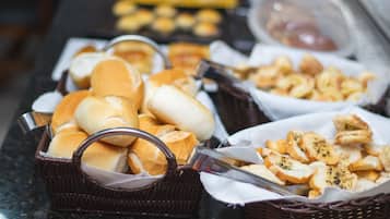 Buffet com diversos alimentos, incluindo pão, doces e frutas fatiadas.