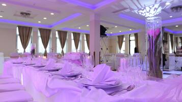 Salão de banquetes com mesas montadas para um evento formal, com toalhas roxas e centros de mesa em vidro transparente.
