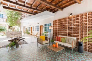 Uma área externa ampla com teto de madeira, piso estampado, sofá com almofadas, mesa de centro e uma placa com a inscrição "QUINTA Margarita BOHO CHIC HOTEL".