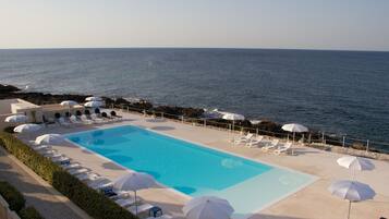 Área de piscina com espreguiçadeiras e guarda-sóis, com vista para o mar.