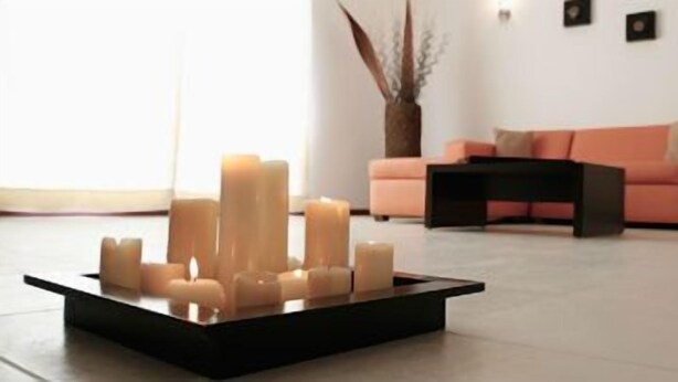 Uma sala de estar moderna com uma mesa de centro preta com várias velas, um sofá rosa e um vaso alto com galhos.