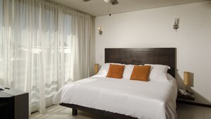 Cama bem arrumada com almofadas brancas e laranja, cabeceira escura e duas luminárias de cabeceira.