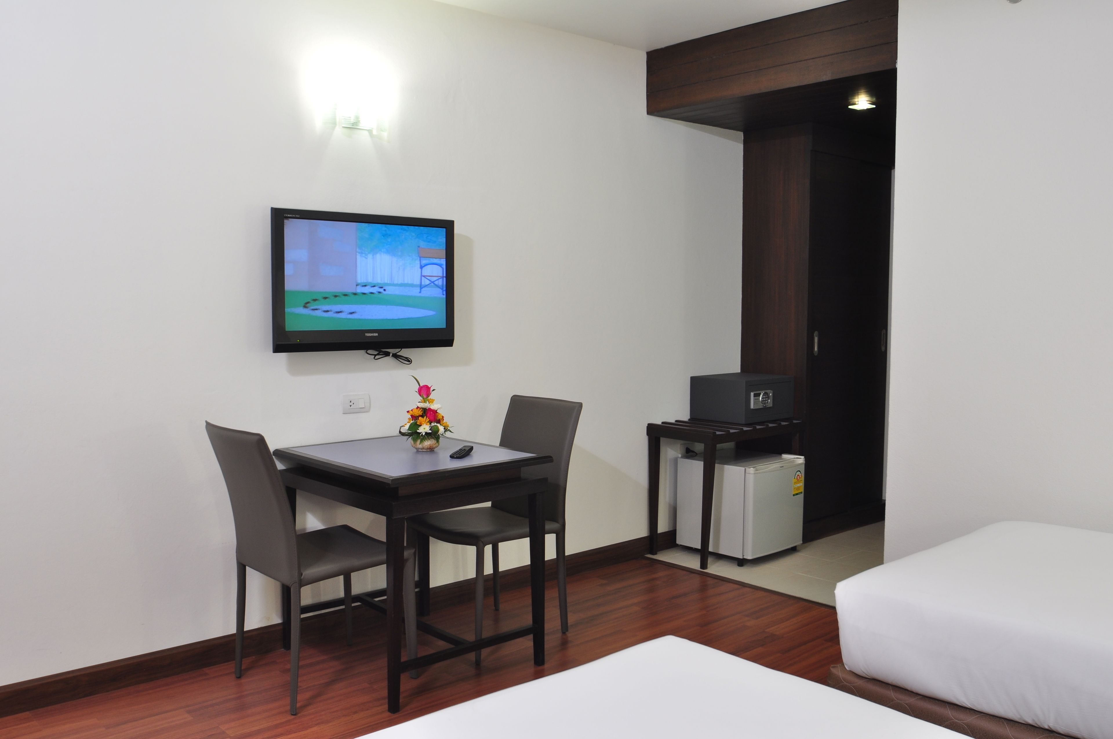 Quarto de hotel com televisão na parede, uma mesa pequena com duas cadeiras, um frigorífico e uma cama.