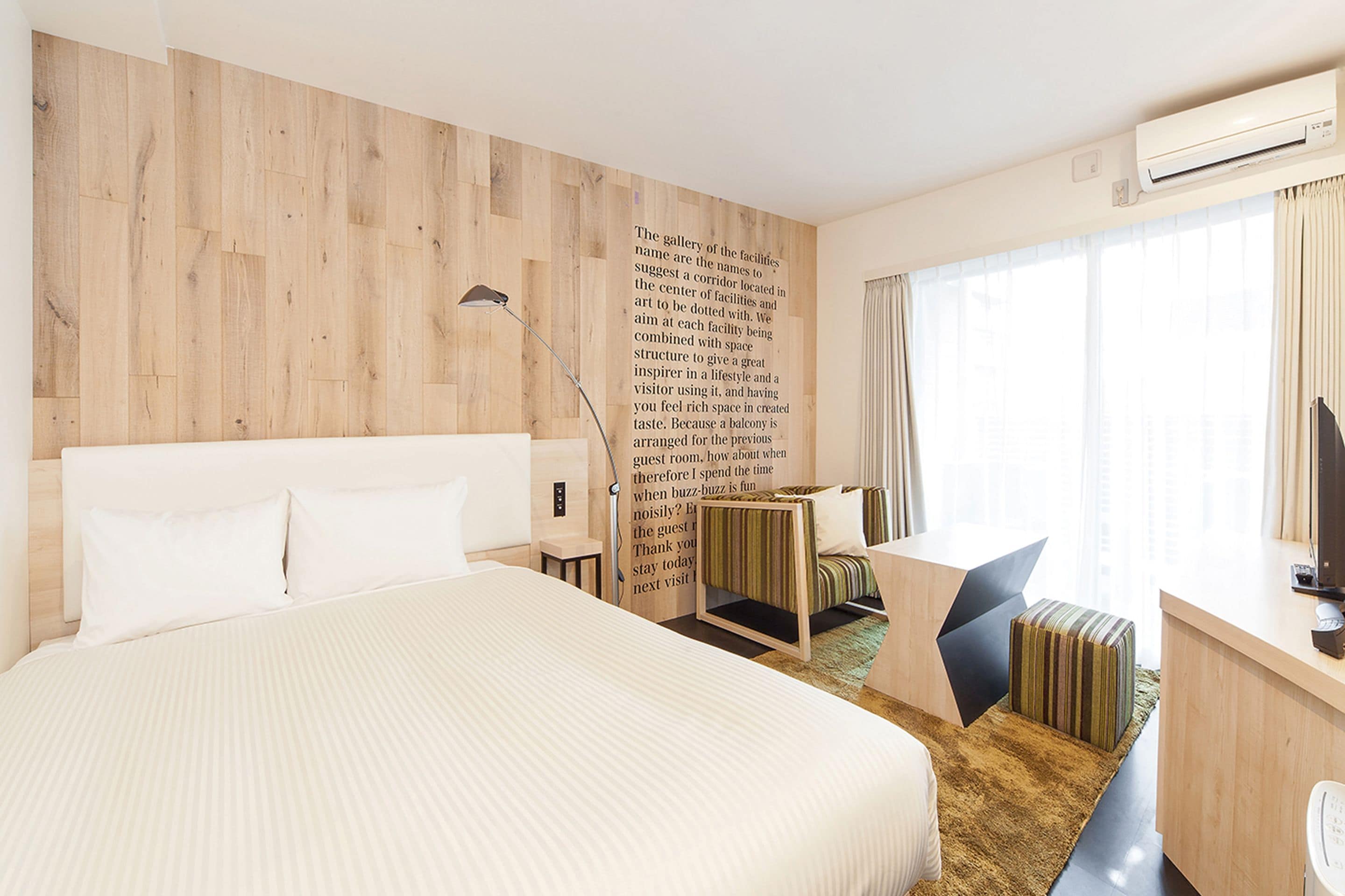 Quarto de hotel com cama grande, escrivaninha, cadeira, televisão e janela com cortinas.