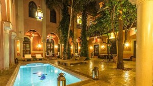 Uma área de piscina com espreguiçadeiras, piscina e um pátio com árvores e colunas.