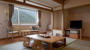 Quarto de hotel com uma mesa de jantar de madeira, cadeiras, uma televisão e vista para uma paisagem montanhosa.
